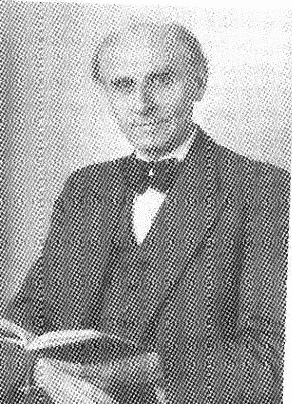 A photo of a person who sits wearing a coat with a bow tie. He holds an open diary.