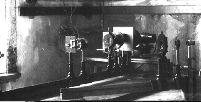 A photograph of equipment It consists of an optical bench on a table with lenses attached to guide rails at different angles.
