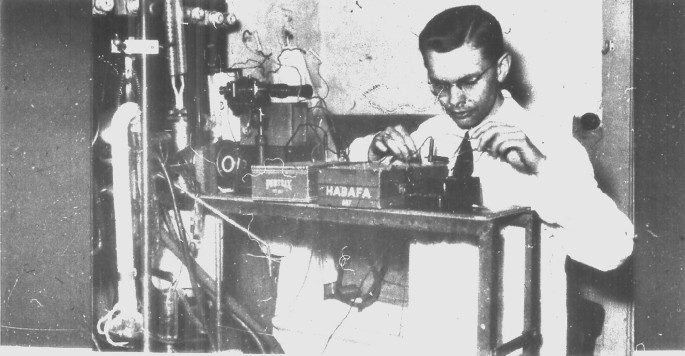 A photo of a person who wears glasses and works on a machine by holding its wires.